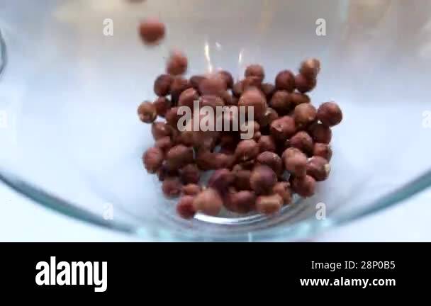 Nuts falling down from the transparent glass bowl on white background ...