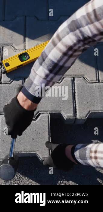 Close-up of a construction worker placing an interlocking paver on sand ...