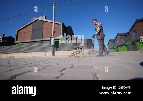 A worker operates a plate compactor on newly laid paving stones in a ...