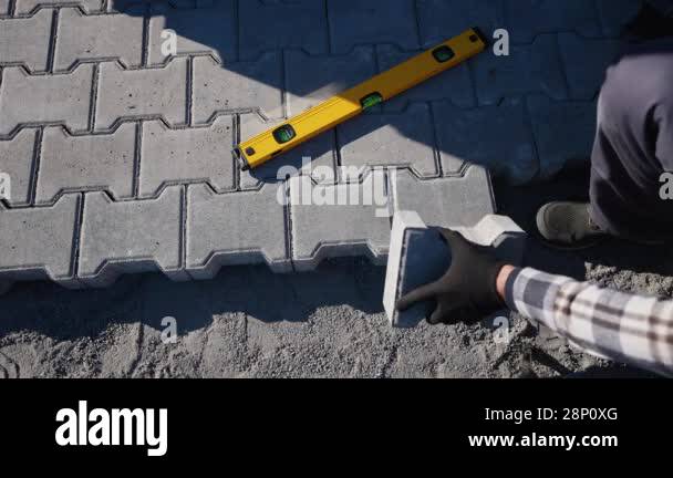 Close-up of a construction worker placing an interlocking paver on sand ...