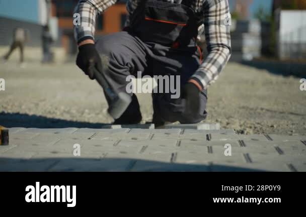 Close-up of a construction worker hammering paving stones into place ...