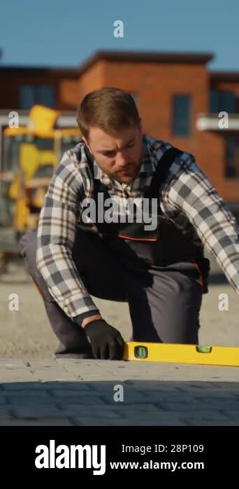 A construction worker kneels to adjust paving stones using a rubber ...