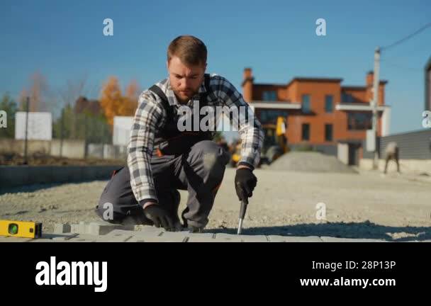 Focused construction worker kneeling and using a leveling tool to align ...