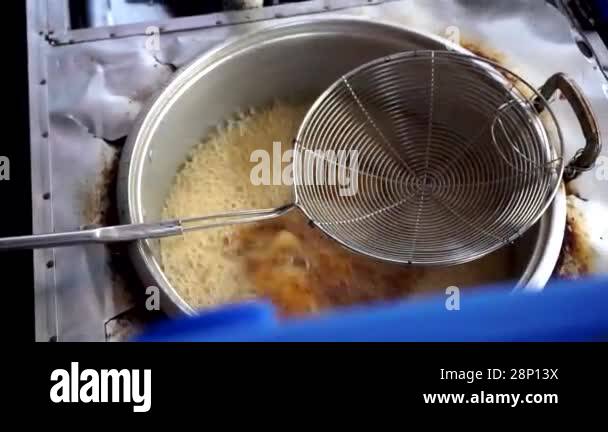 A deep frying process with a metal strainer in a pot of bubbling oil ...
