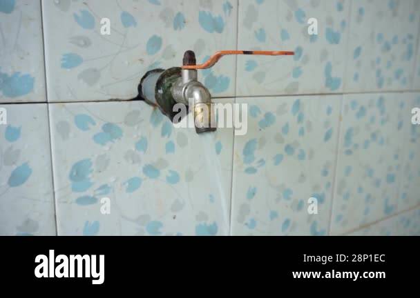A water faucet with a red handle is mounted on a tiled wall, with water ...