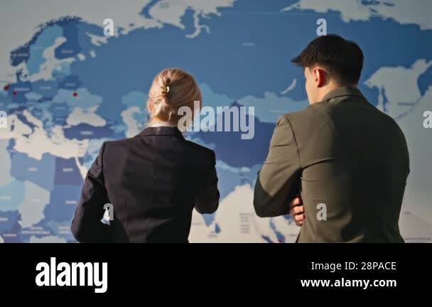 Two analysts discussing world map in monitoring office back view. Professional employees working ...