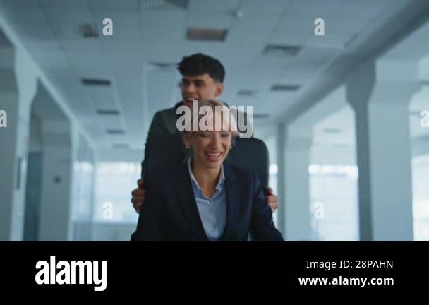 Laughing businesswoman enjoying riding office chair with man colleague ...