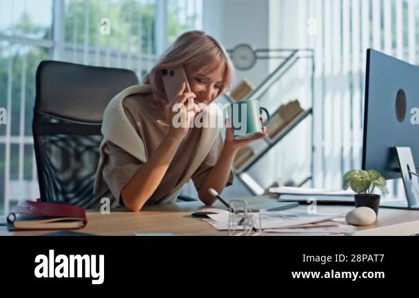 Relaxed lady boss calling smartphone drinking espresso at work break ...