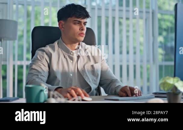 Frowning guy texting pc keyboard working computer in open space office ...