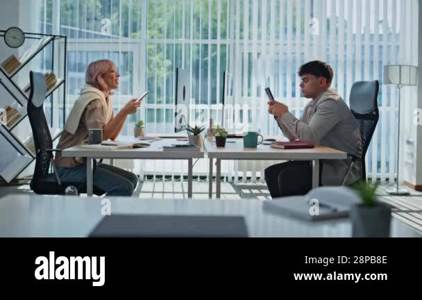 Relaxed colleagues using cellphones sitting office desk together ...