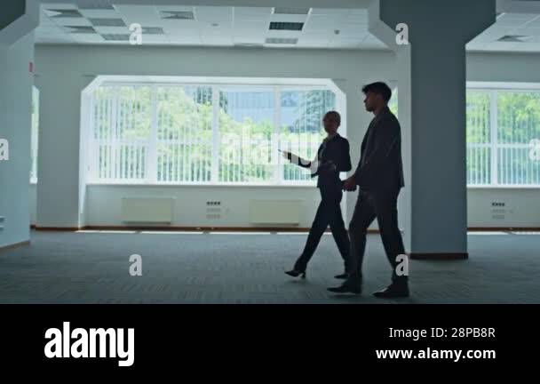 Formal suits colleagues crossing empty hall. Focused businesspeople going to work chatting ...
