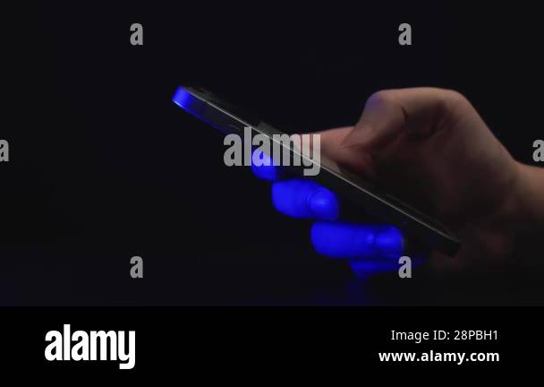 Close-up of a hand interacting with a smartphone in a dark room ...
