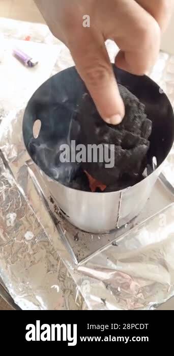 Man arranges pieces of charcoal in a metal cylinder, base of a smoking ...