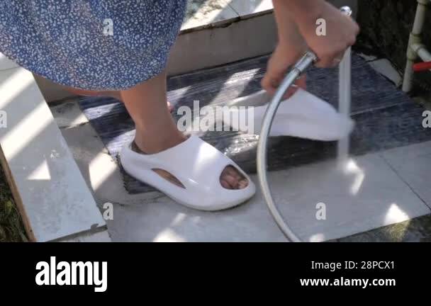 Washing feet and sandals in backyard using a hose on a warm day. Woman ...