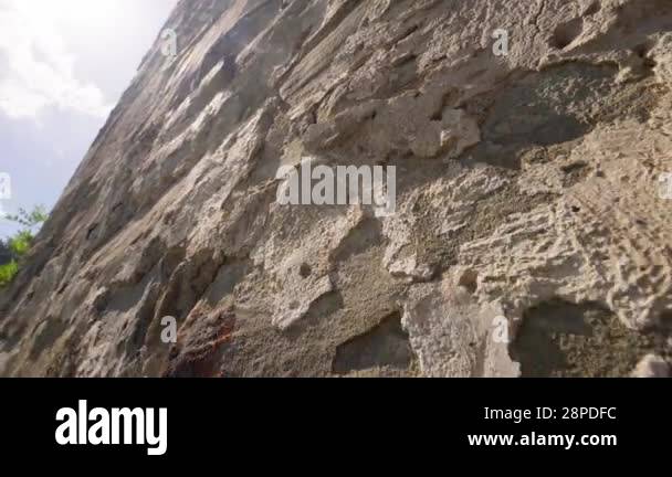 Sunlight illuminates tall stone wall, its textured surface revealing ...