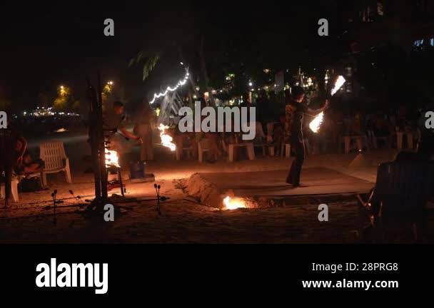 A performer manipulates flaming props on a beach stage at night ...