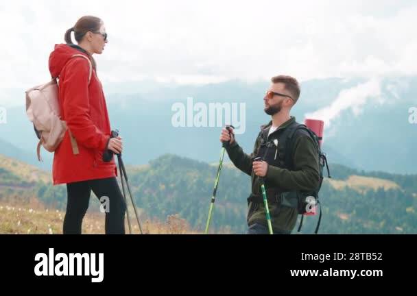 Hikers man and woman talking in mountains with sticks in hands ...