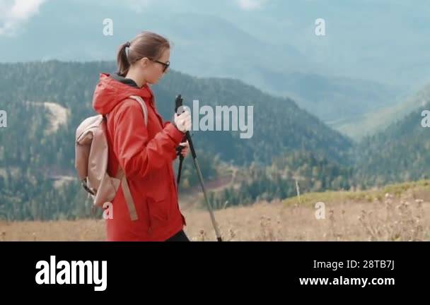 Woman hiker hiking in mountains walking on slope on path holding sticks ...