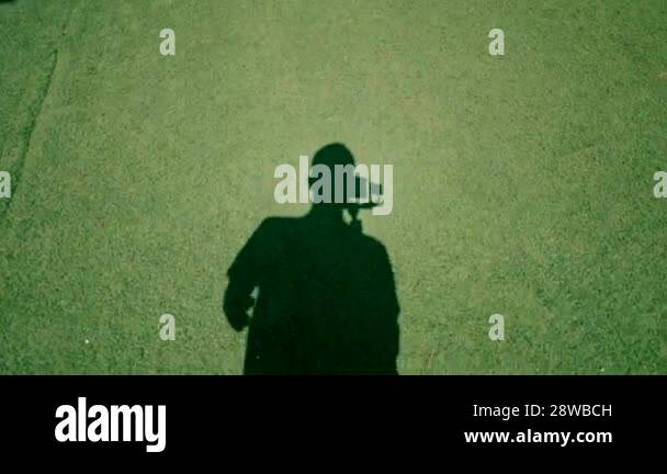A shadow on the grass of a photographer walking, holding a camera in a ...