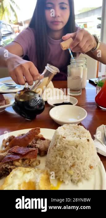 young Filipina woman in a Filipino traditional food restaurant pours ...