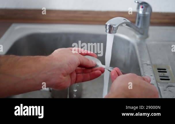 A person diligently and carefully cleaning numerous utensils under a ...