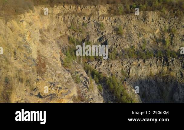 Rocky cliff with rough textures, golden sunlight, and sparse vegetation ...
