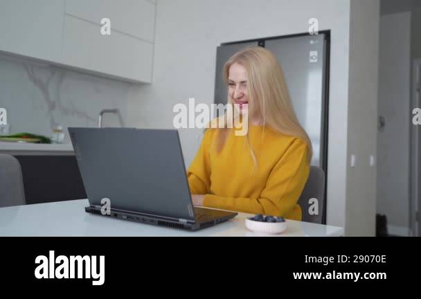A blonde female professional is working on a laptop and taking notes in ...