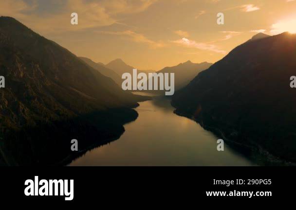 Witness the serene beauty of Plansee lake Austria as the sun sets behind majestic mountains. The ...