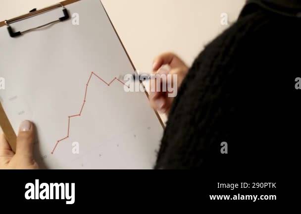 Close up of female hands studying and pointing a line diagram on paper ...