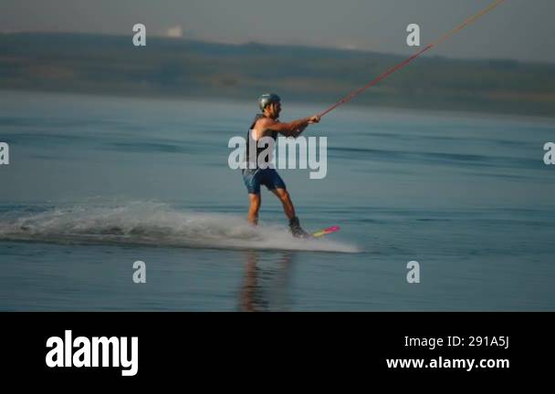 male wakeboarder wakesurfing at sunrise. man riding on waterski cable ...