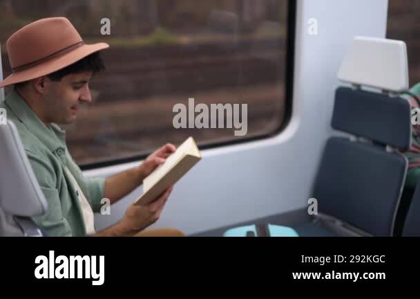 relaxed traveler reading a book on the train, sitting next to their ...
