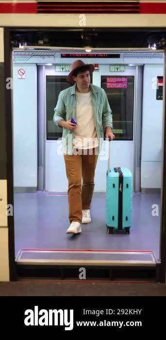 vertical smiling traveler checks their smartphone while getting off the train with luggage at ...