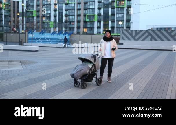 A mother takes a stroll with her baby in a stroller through a spacious urban plaza. The early ...