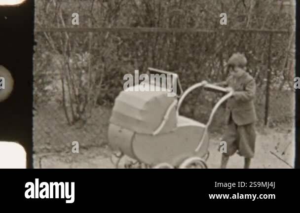 8mm shot of a young boy strolling and pushing a baby pram along a ...