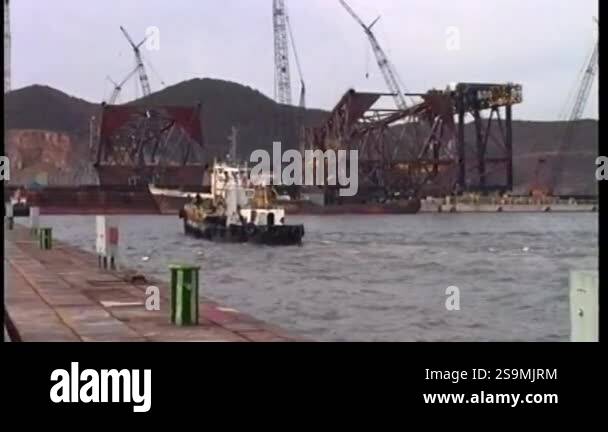 A retro home video captures a shipyard with a small tugboat moving ...