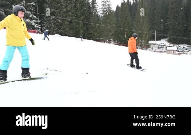 Two snowboarders glide down a gentle slope in a snow-covered mountain ...
