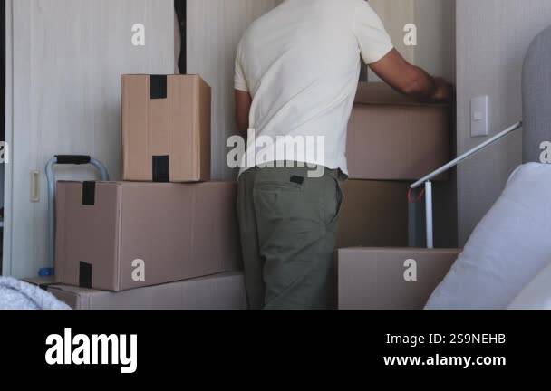 A man is standing in a room with boxes and clothes. He is reaching for ...
