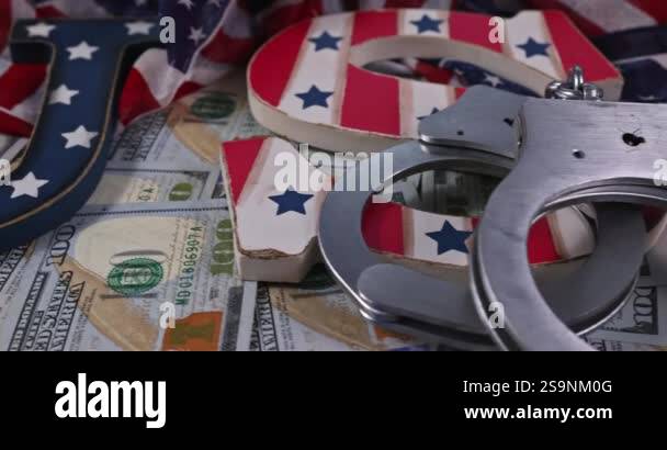 A close-up of handcuffs, dollar bills, and red, white, and blue letters ...