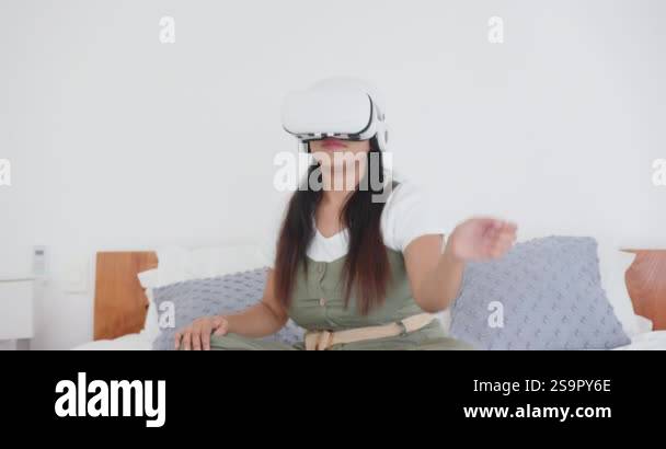 Using VR headset, asian woman sitting on bed in relaxed spa environment ...