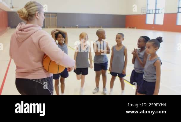 In school gym, coach guiding children playing basketball, enjoying ...