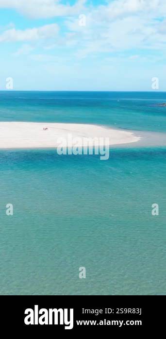 A small, white sandbar extends into turquoise water. Three figures in ...
