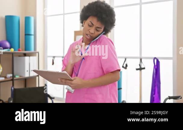 A professional african american woman in pink scrubs multitasks at work ...