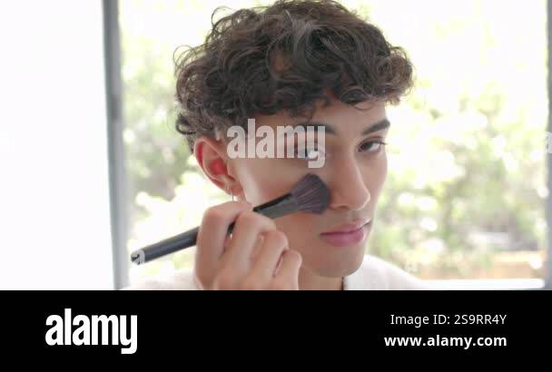 Applying makeup with brush, non binary person focusing on face in home ...