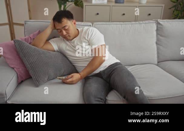 A young chinese man lounging on a couch in a cozy living room ...