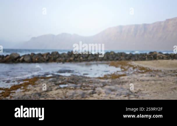 Blurred beach landscape with rocky shore and distant mountains in ...