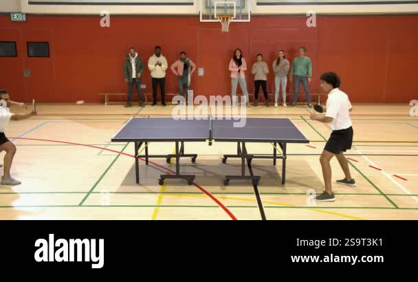 Playing table tennis, two men competing in school gymnasium with ...