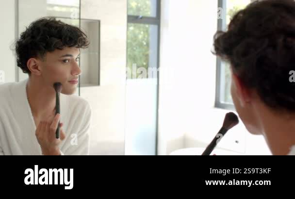 Applying makeup, non binary person using brush while looking in ...