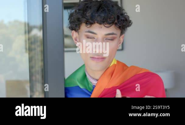 Wearing pride flag, non binary person standing by window, looking ...