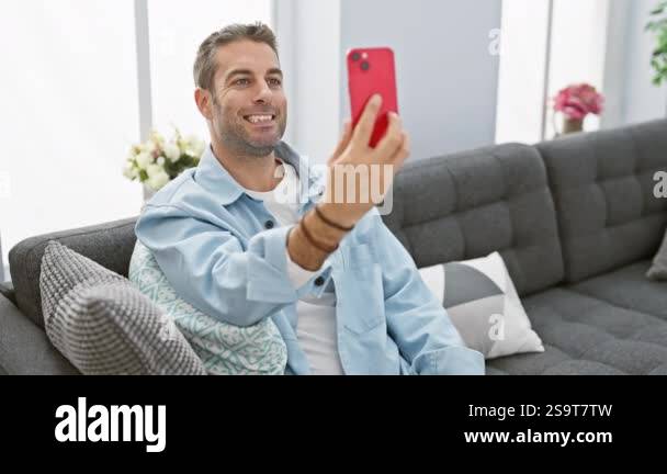 Handsome young man taking a selfie with a smartphone in a modern living ...