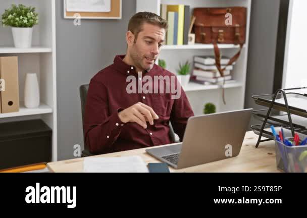 A focused man working in an organized office room with laptop, pen, and ...